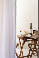 Uma mesa de madeira redonda com uma garrafa de vinho, duas taças, uma tigela de bolachas e um prato com queijo e carne.