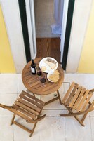 Uma mesa de madeira com uma garrafa de vinho, copos e um prato de queijo e biscoitos. Duas cadeiras de madeira estão dispostas ao redor da mesa.