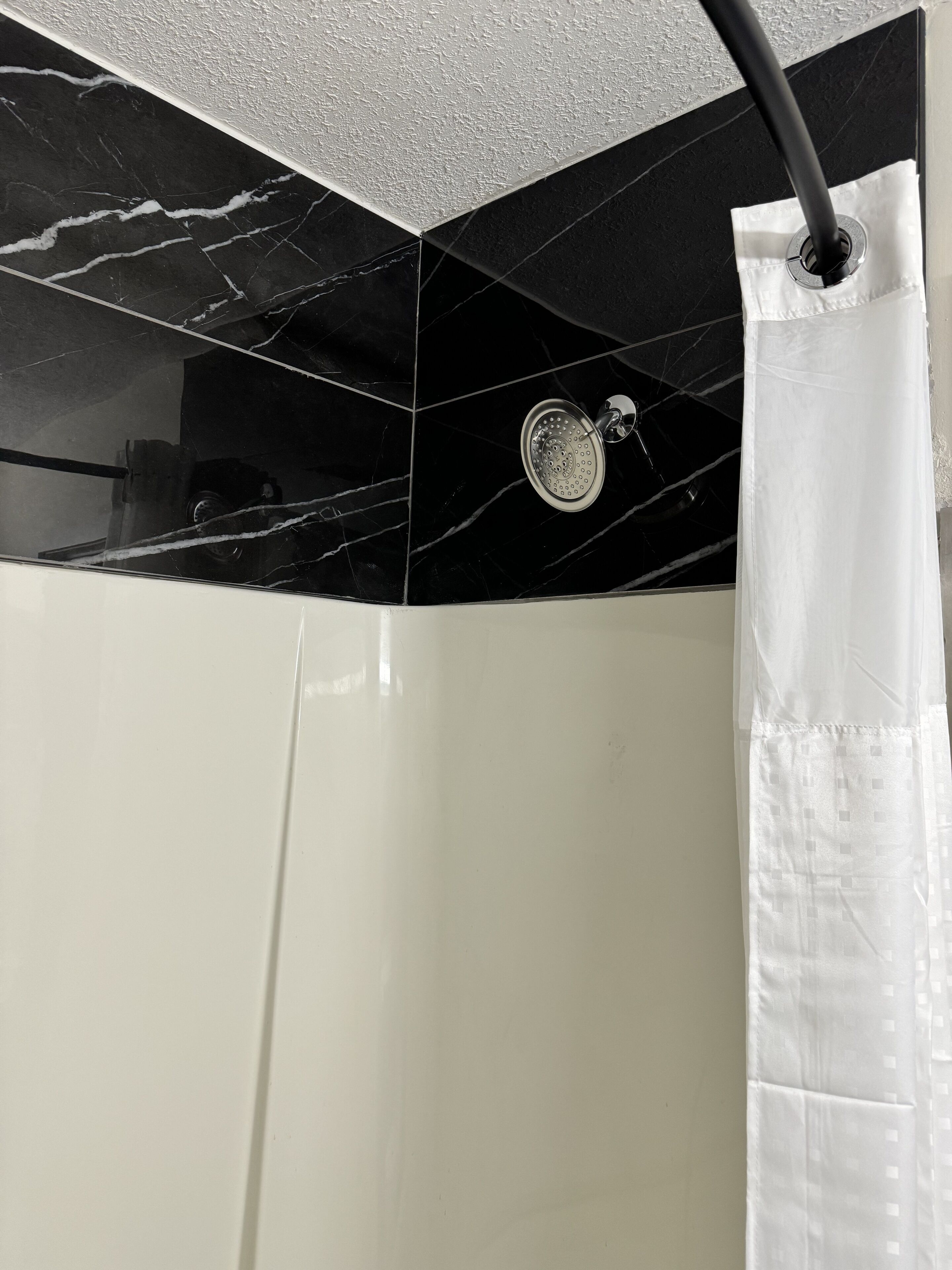 Canto de um banheiro com azulejos preto e branco, um chuveiro e um box branco.
