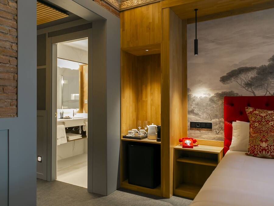 Quarto de hotel com um armário de madeira, uma cama com cabeceira vermelha e uma obra de arte na parede.