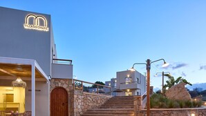 Um edifício moderno com uma escadaria de pedra que leva a uma porta de madeira, uma área de recepção com móveis de vime e um grande afloramento rochoso no jardim.