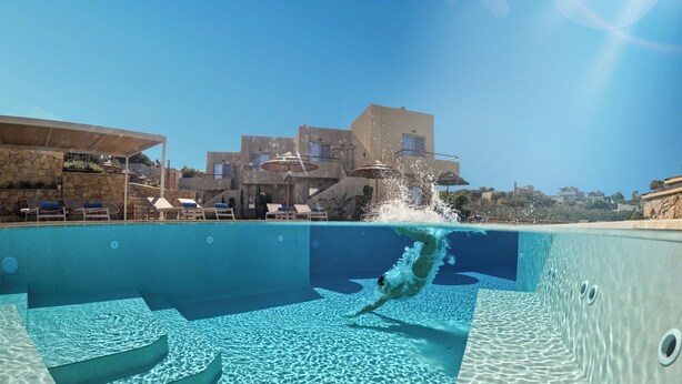 Piscina cristalina com prancha de mergulho e espreguiçadeiras, cercada por edifícios.
