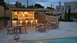Uma área de bar ao ar livre com paredes de pedra, móveis de madeira e uma piscina.