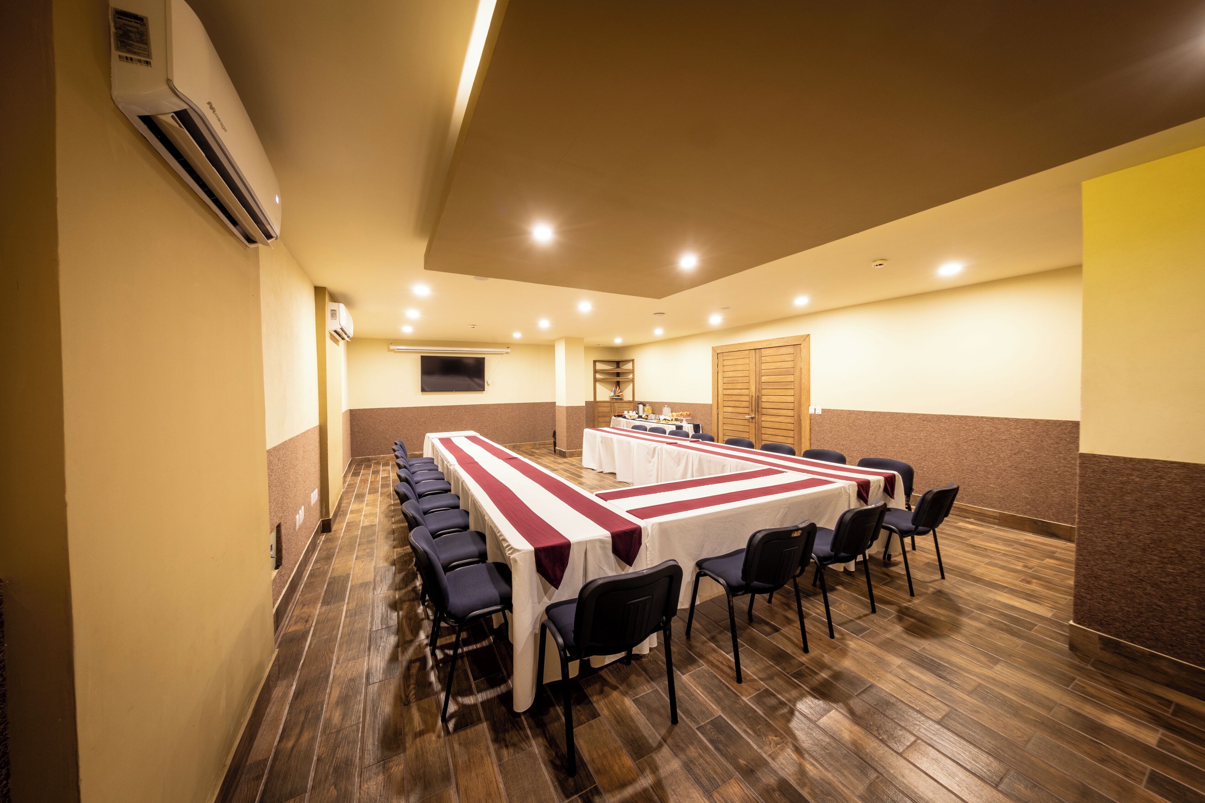 Uma sala de conferências com uma mesa comprida, cadeiras e um aparelho de ar condicionado.