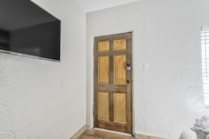 Quarto com porta de madeira, TV de tela plana montada e janela com persianas.