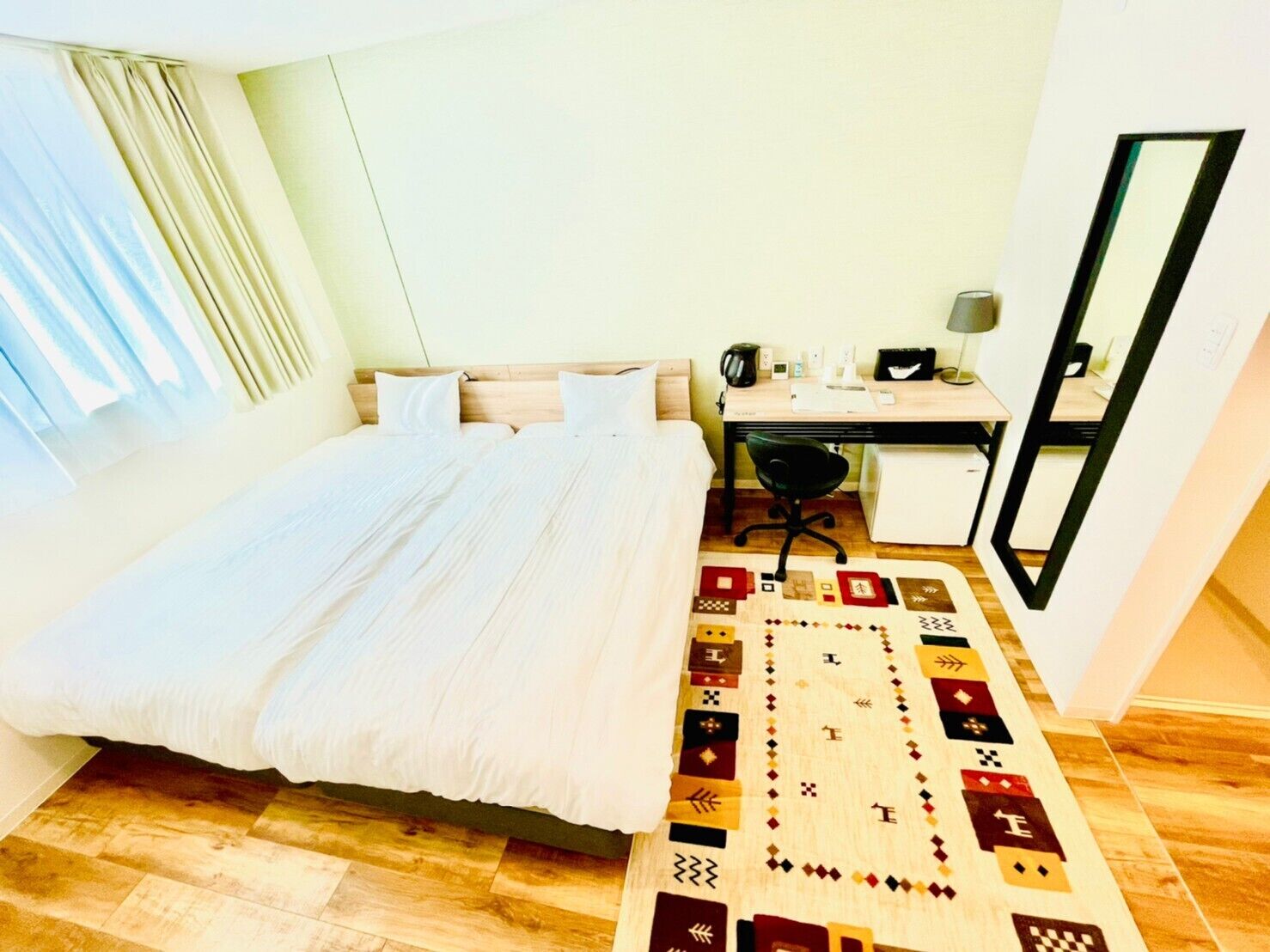 Quarto de hotel com cama, escrivaninha, cadeira, espelho e tapete estampado.