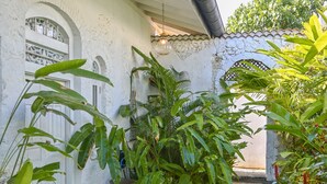 Um pátio com caminho de pedras, um edifício branco com porta e vegetação exuberante.