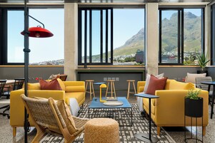 Um interior moderno com sofás amarelos, uma poltrona de vime, uma mesa de centro e vista para uma montanha.