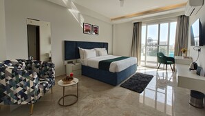 Quarto de hotel moderno com uma cama grande, uma escrivaninha, uma cadeira, uma pequena mesa com um cesto e vista para a varanda.