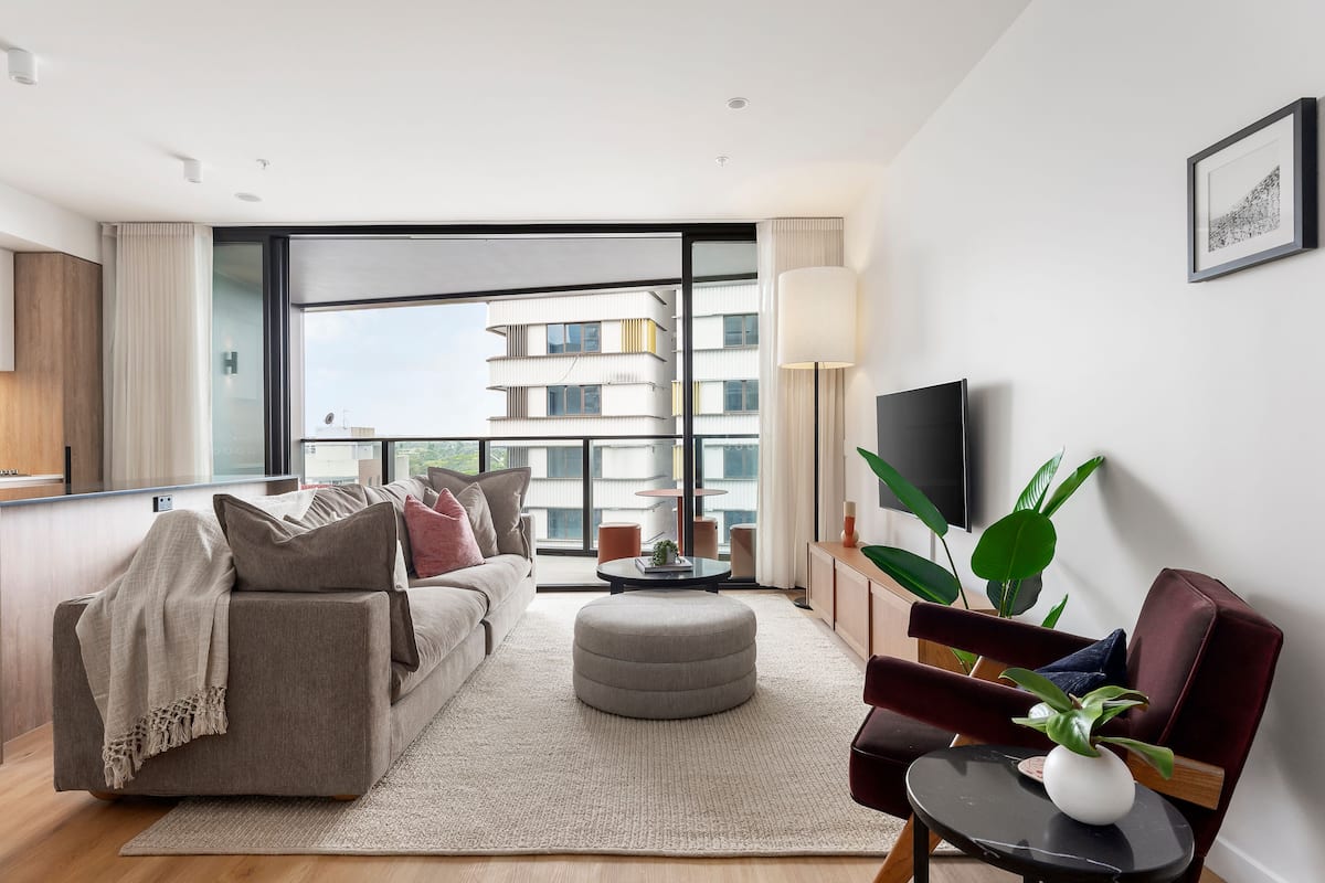 Uma sala de estar moderna com sofá, apoio para os pés e uma TV em um móvel.