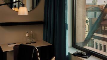 Quarto de hotel com escrivaninha, cadeira e janela com vista para edifícios.