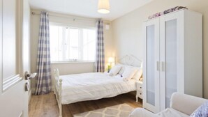 Quarto com uma cama, guarda-roupa, mesa de cabeceira e janela com cortinas.