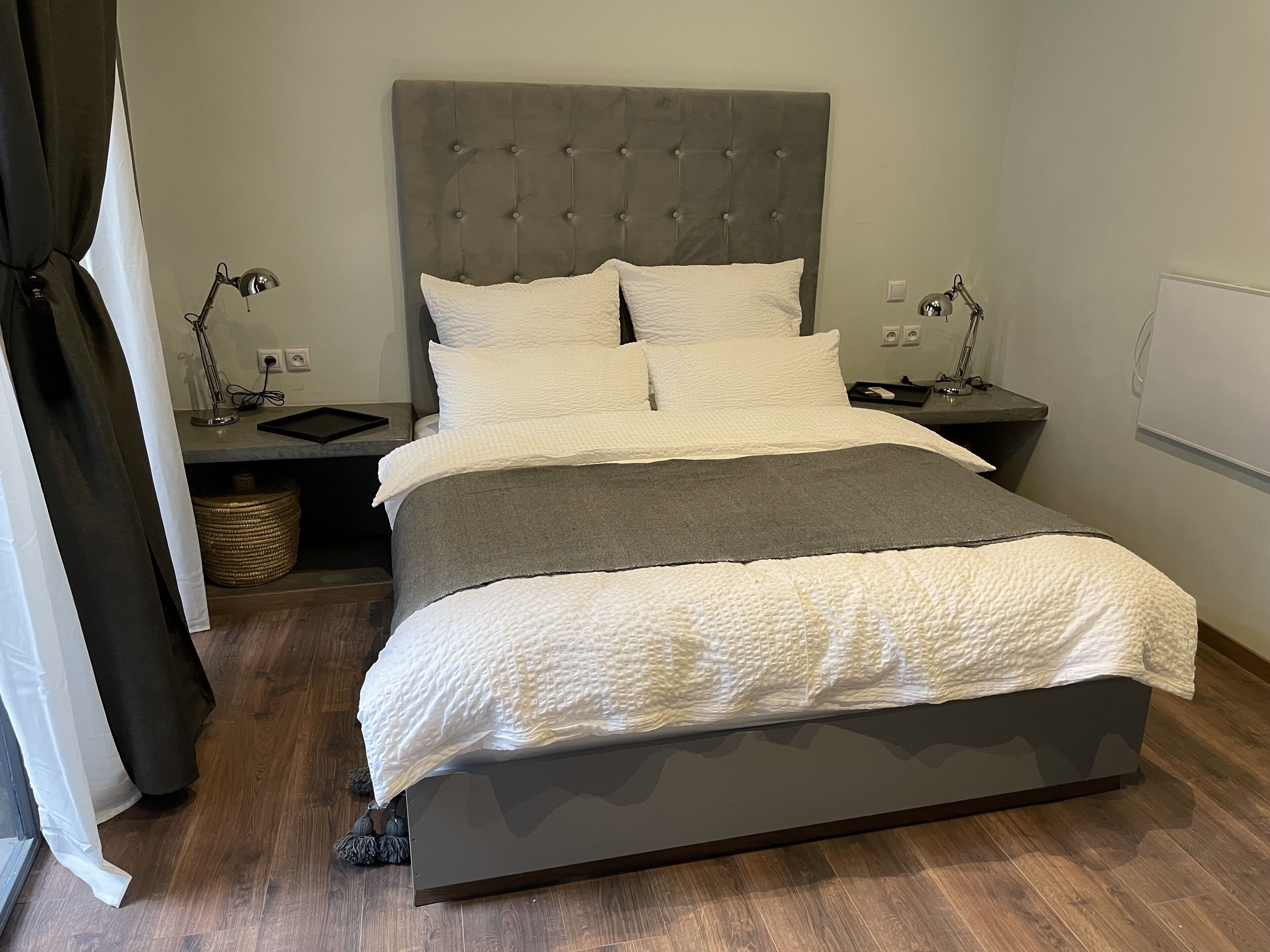Quarto moderno com cama grande, cabeceira estofada cinza e mesas de cabeceira com abajures.