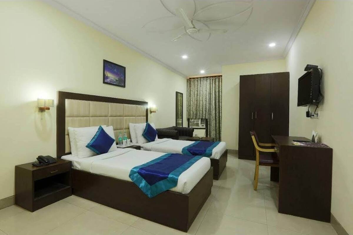 Quarto de hotel com duas camas, uma escrivaninha, uma cadeira, uma televisão e um ventilador de teto.