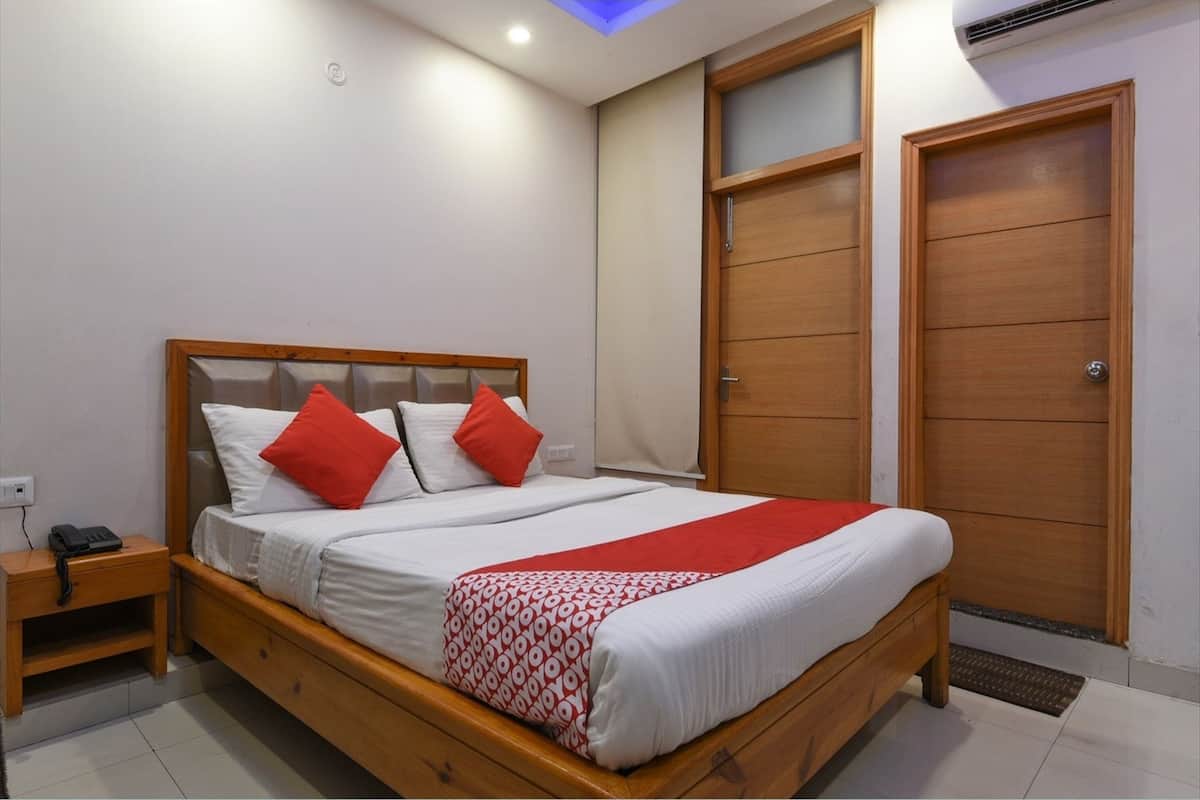 Cama bem arrumada com estrutura de madeira, mesa de cabeceira com um telefone e manta com padrão vermelho e branco.