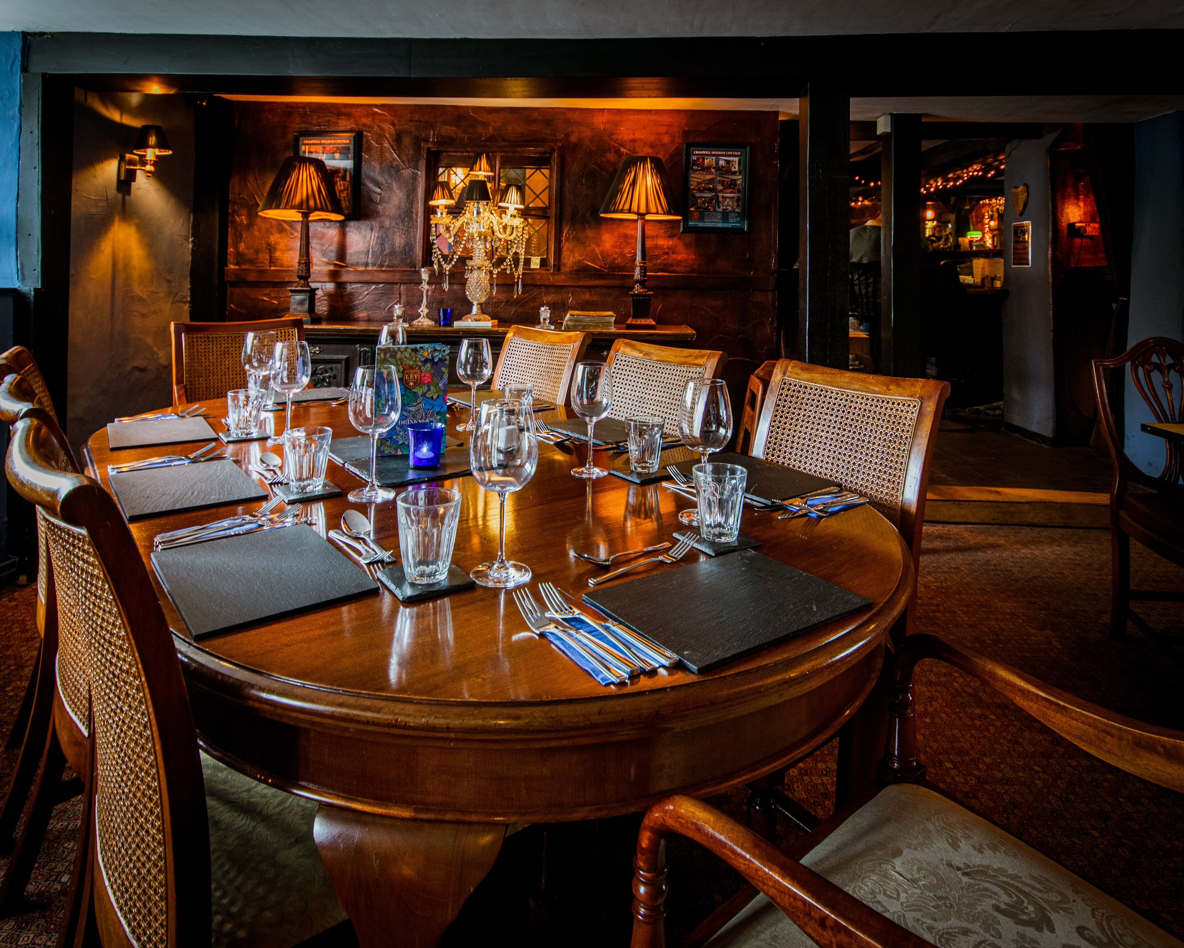 Mesa de jantar posta para seis lugares, com cadeiras, lustre e luminárias fixadas na parede.