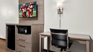Quarto moderno com TV de tela plana fixada na parede, escrivaninha com cadeira e micro-ondas integrado.