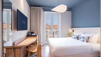 Quarto de hotel com cama, escrivaninha, cadeira, espelho e janela.