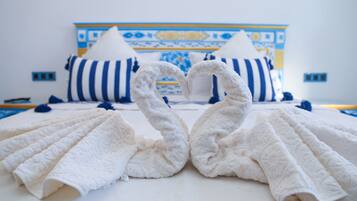 Cama com toalhas brancas dispostas em forma de cisnes, almofada listrada em azul e branco, e cabeceira azul e amarela.