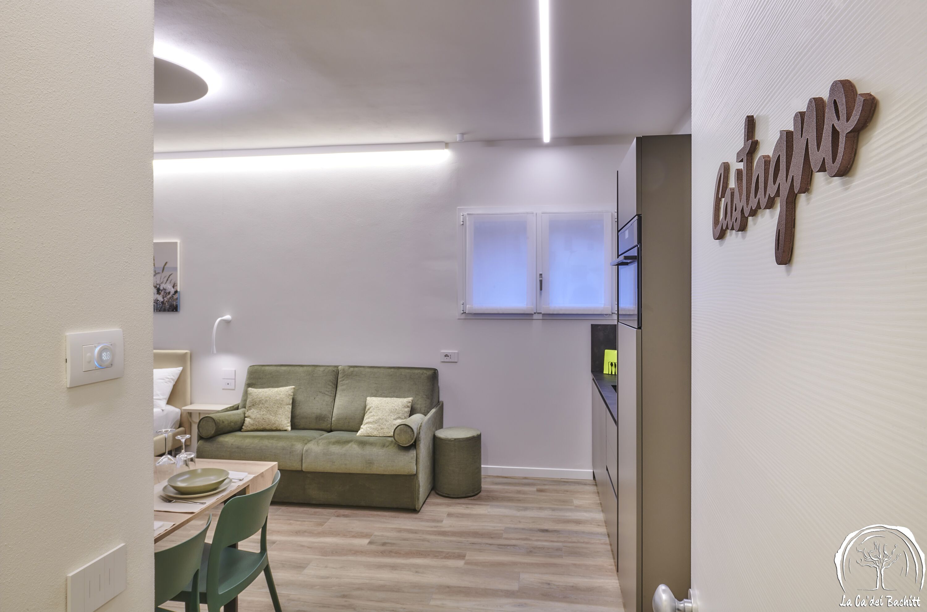 Uma sala moderna com um sofá verde, uma mesa de jantar com cadeiras e uma cozinha com armários e bancada.