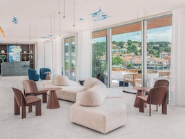 Uma sala de estar ampla com um sofá grande, várias poltronas e vista para uma cidade através de grandes janelas.