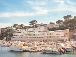 Marina com vários barcos atracados, um edifício com a inscrição 'BLEU' ao fundo e céu claro.