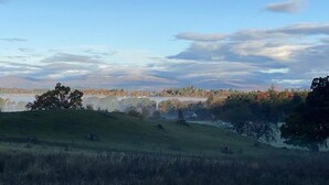 Paisagem com colinas ondulantes, árvores e uma massa de água ao longe.