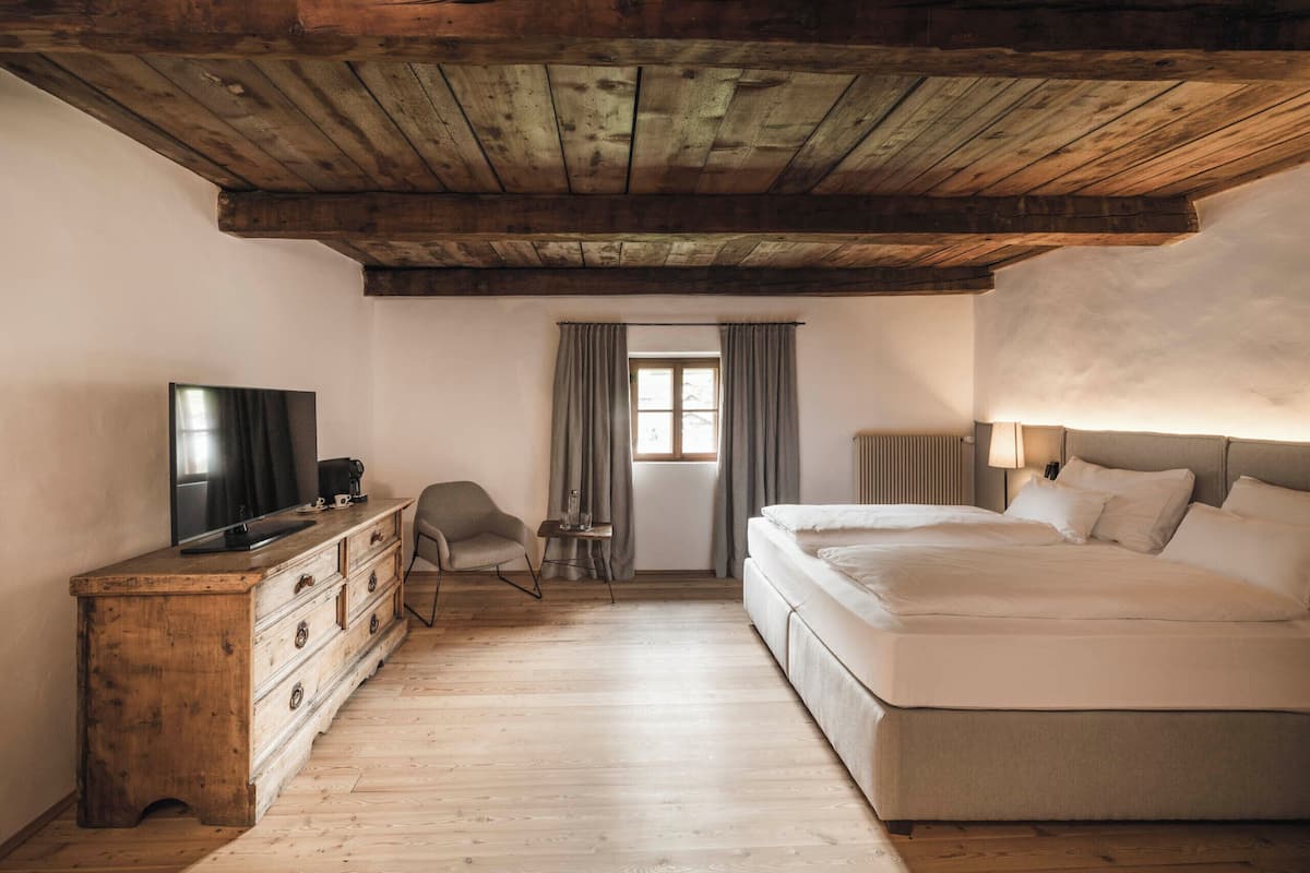 Quarto com teto de madeira, cama, cômoda, televisão e janela com cortinas.