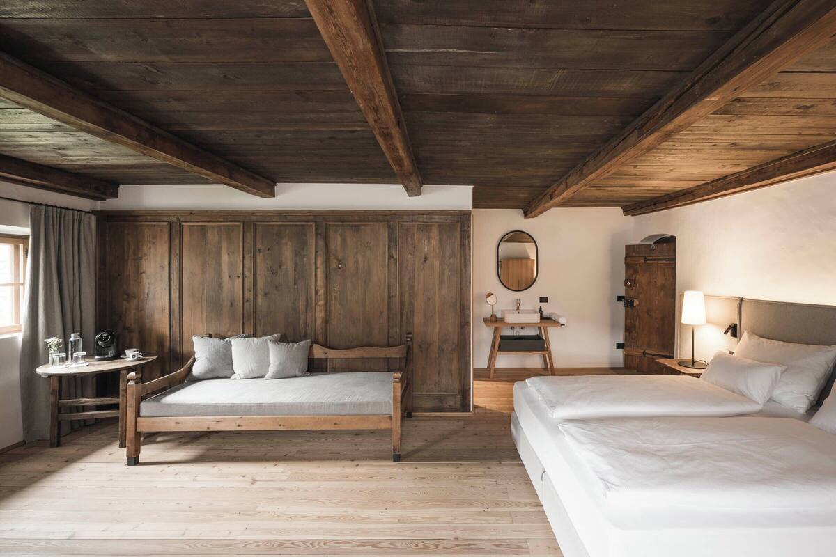 Quarto rústico com vigas de madeira, guarda-roupa de madeira, mesa de cabeceira com abajur e duas camas.