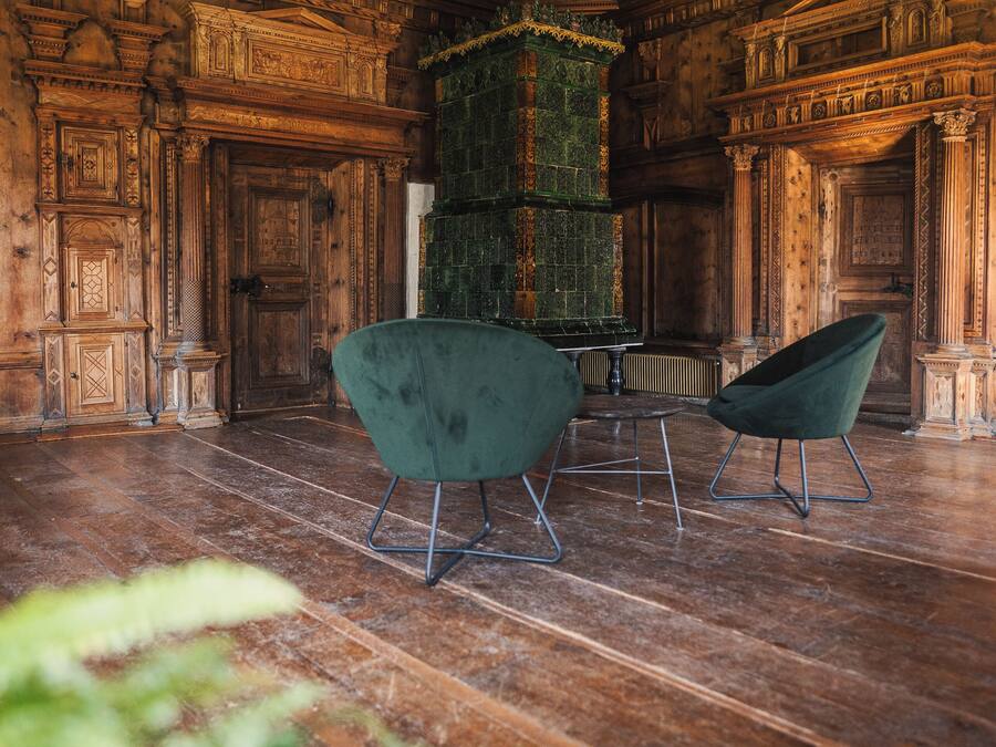 Quarto espaçoso com painéis de madeira, uma grande poltrona verde e uma mesa.