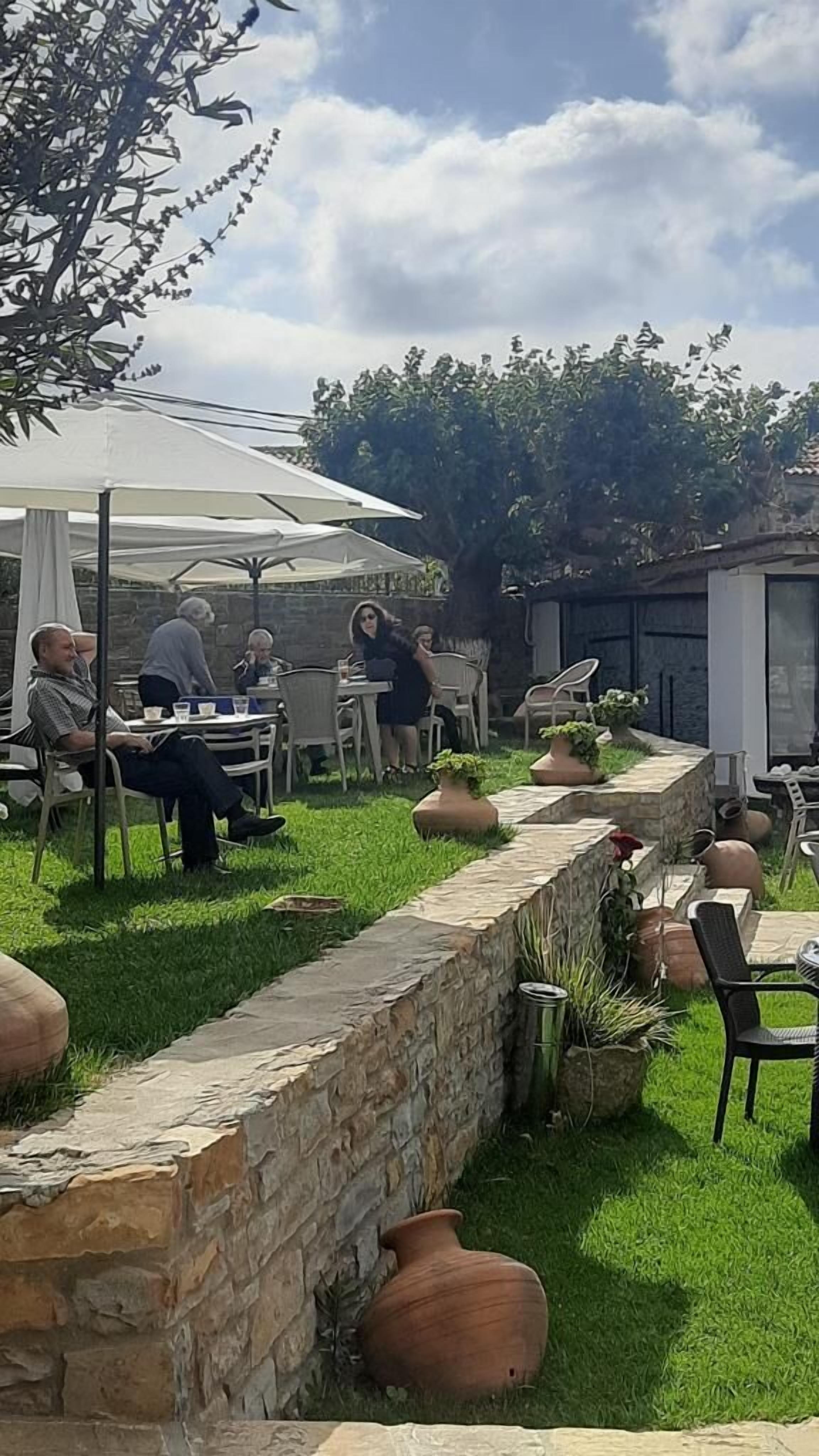 Uma área externa com mesas e cadeiras sob um toldo branco, cercada por paredes de pedra e plantas em vasos.