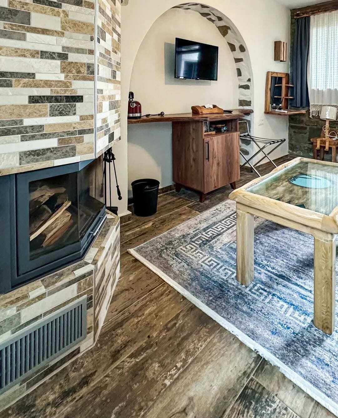 Uma sala de estar aconchegante com lareira de pedra, televisão presa a uma parede em arco, armário de madeira e mesa de centro de vidro.