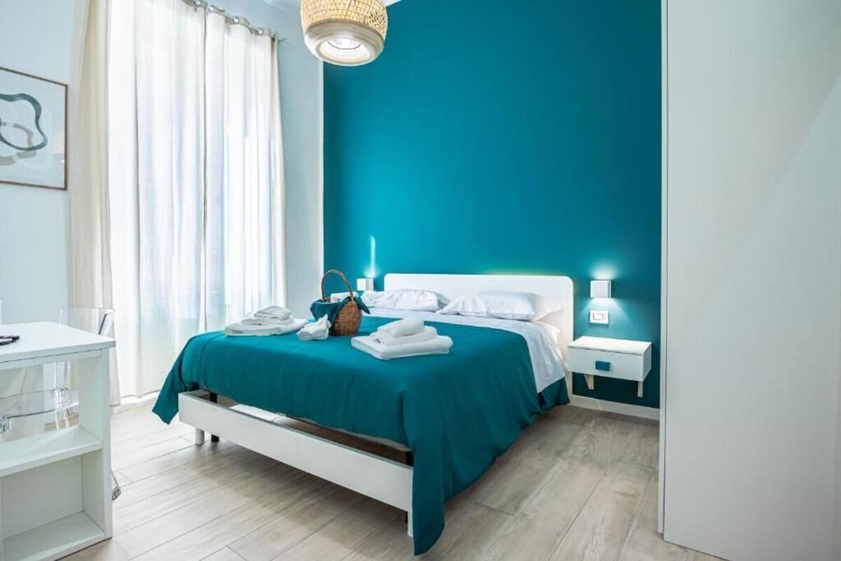 Quarto moderno com parede em tom de verde-água, cama branca e mesa de cabeceira com abajur.