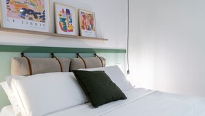 Uma cama com almofadas brancas e verdes, cabeceira verde e duas obras de arte emolduradas acima.