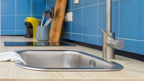 Cozinha com pia de aço inoxidável, backsplash de azulejos azuis e tábua de corte de madeira.