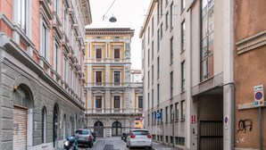 Uma rua estreita com carros e motocicletas estacionados, edifícios com arquitetura clássica e uma placa de proibido estacionar.