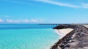 Uma praia com águas turquesa cristalinas, areal arenoso e um píer que se estende para o oceano.