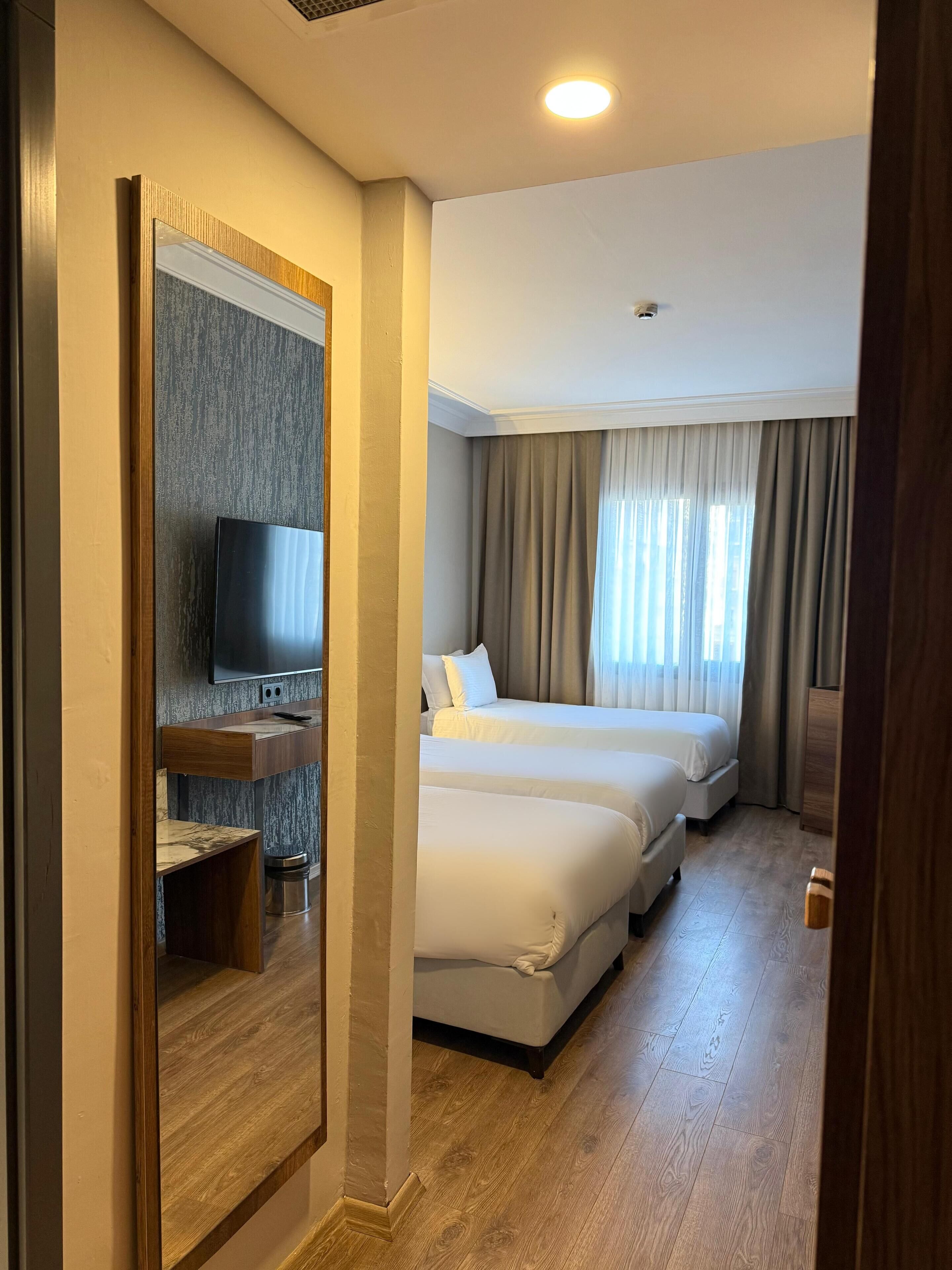 Quarto de hotel com duas camas, televisão, escrivaninha de madeira e espelho.