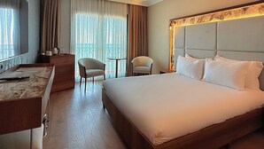 Quarto de hotel com uma cama grande, uma escrivaninha, duas cadeiras e uma mesinha.