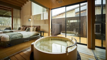 Quarto moderno com uma cama grande, um espaço de estar separado e uma banheira de hidromassagem em vidro.