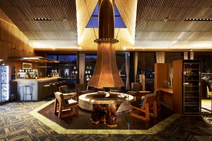 Uma área de bar moderna com uma mesa de madeira central, banquetas e uma luminária pendente grande.