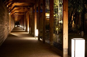 Um corredor com vigas de madeira e paredes de tijolo, conduzindo a uma saída iluminada.