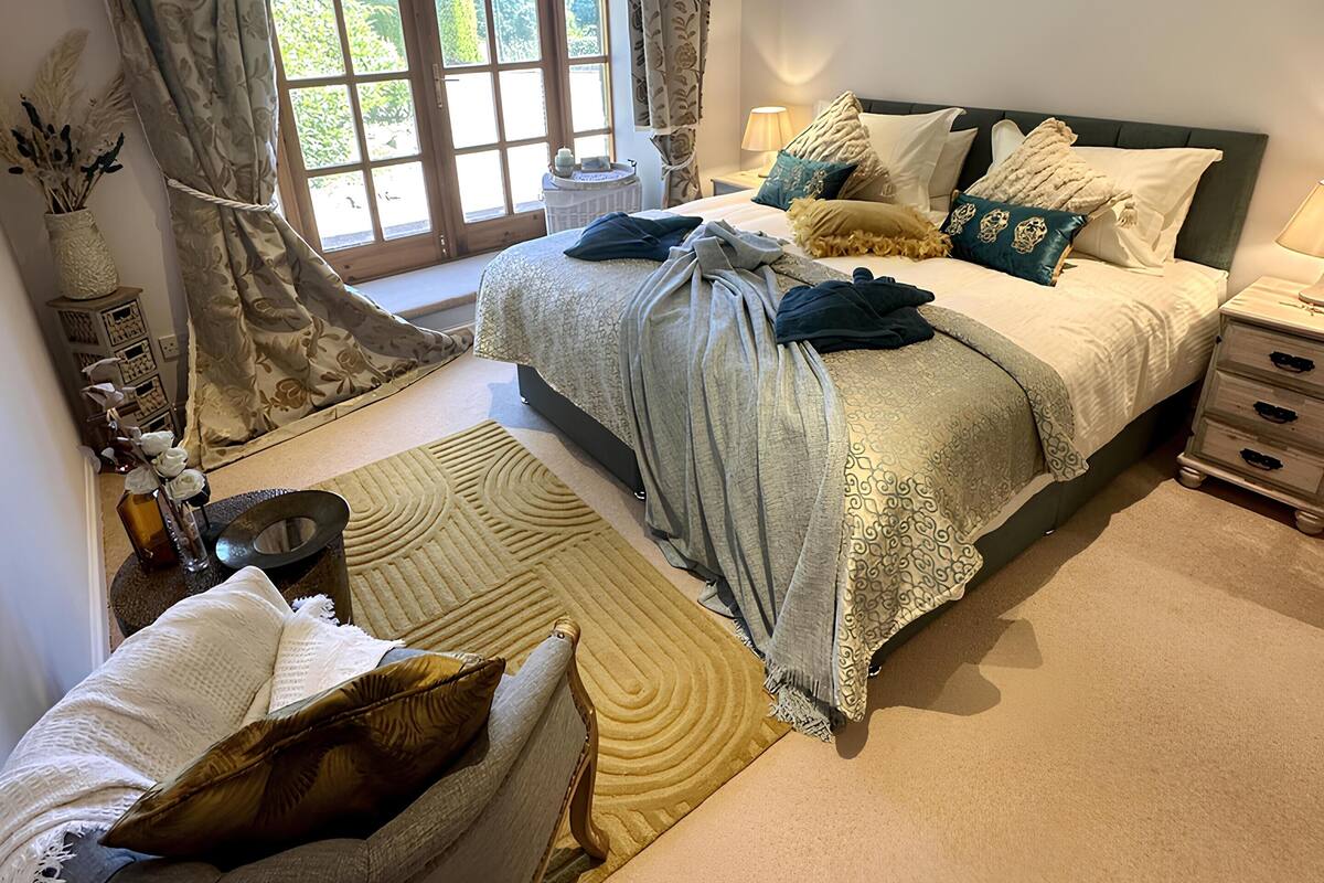 Quarto com uma cama grande, uma cadeira, uma mesa de cabeceira e uma janela com cortinas.