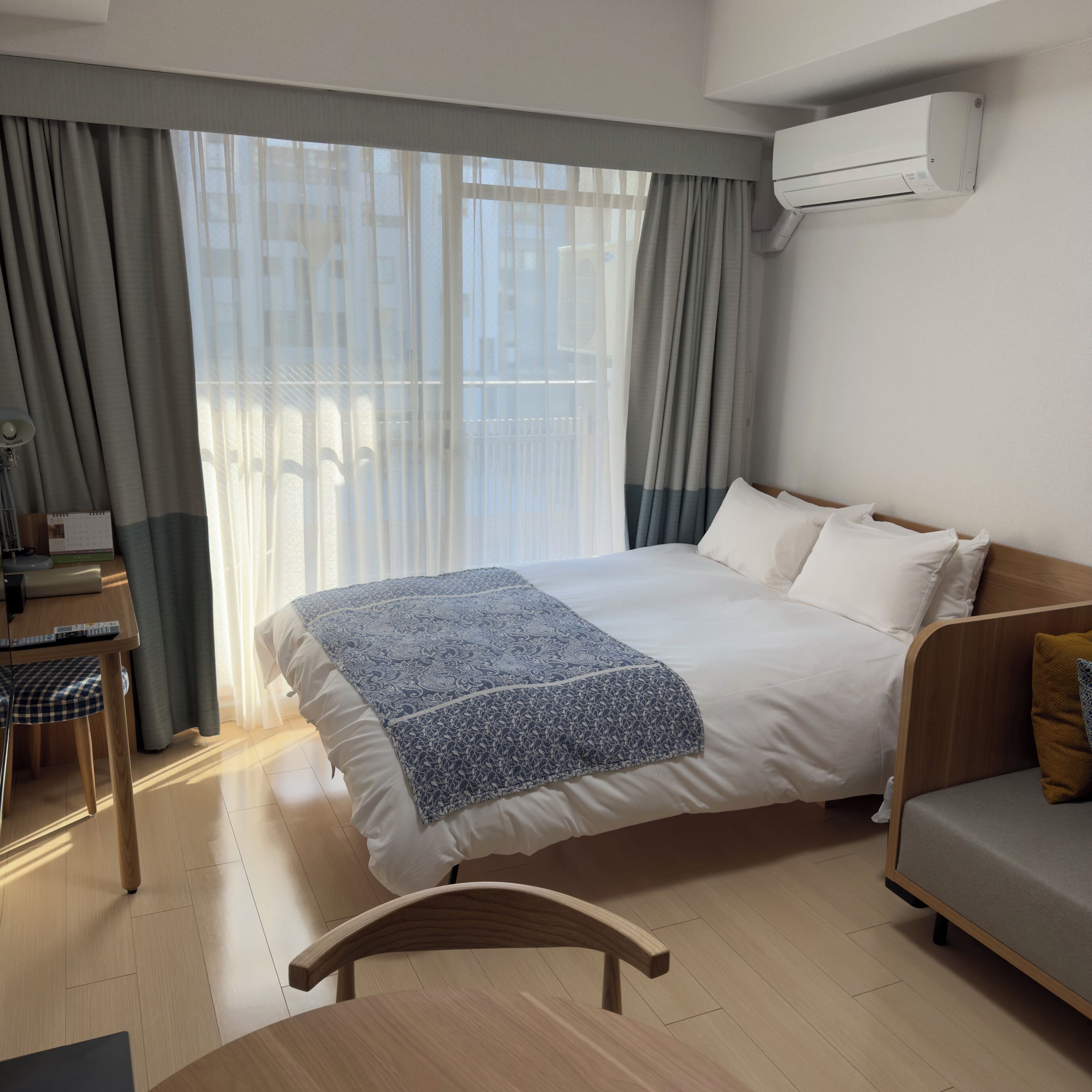 Quarto de hotel com uma cama grande, uma escrivaninha de madeira, uma cadeira, um sofá e um ar condicionado.