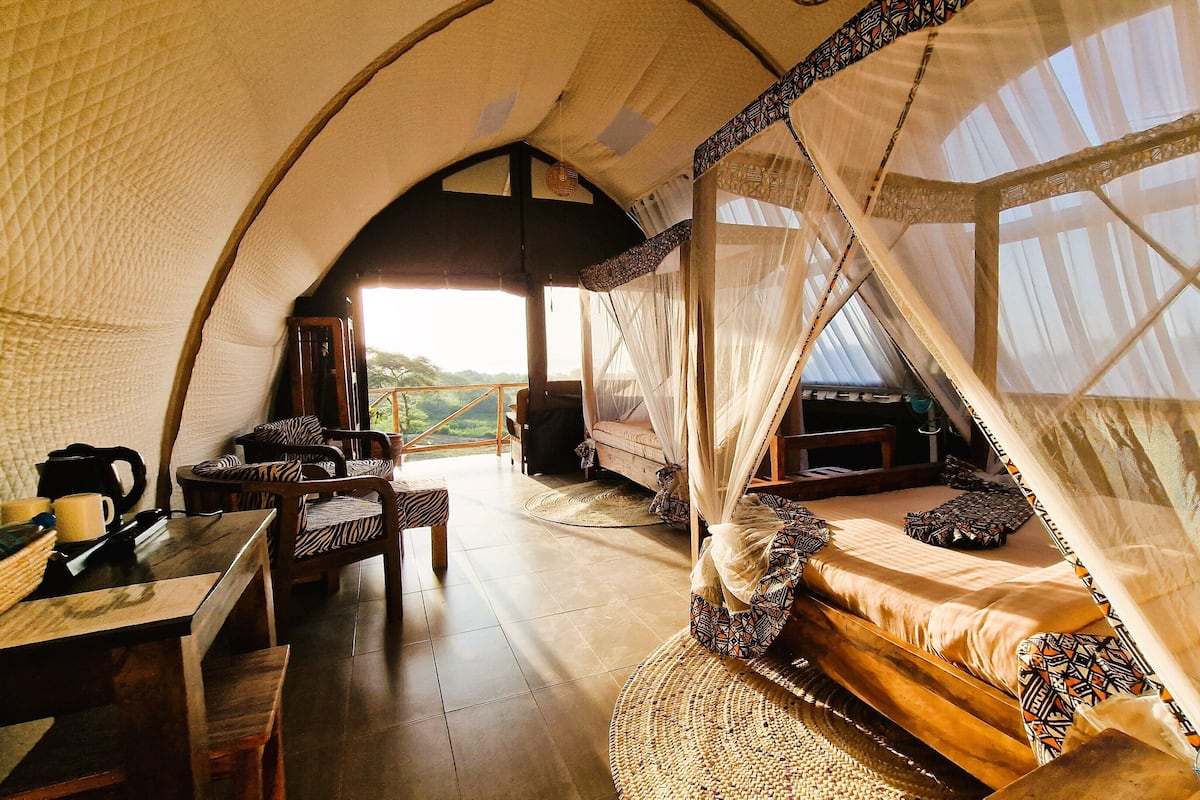 Uma tenda acolhedora e bem iluminada, com cama, mesa e cadeiras, e vista para o exterior.