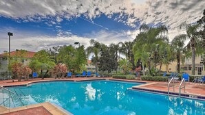 Piscina com água azul, rodeada por palmeiras e cadeiras azuis.
