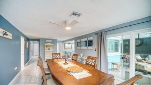 Uma sala de jantar com uma grande mesa de madeira, seis cadeiras e um ventilador de teto.