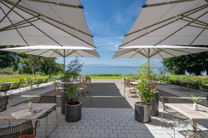 Um terraço com mesas, cadeiras, grandes guarda-sóis e plantas em vasos.
