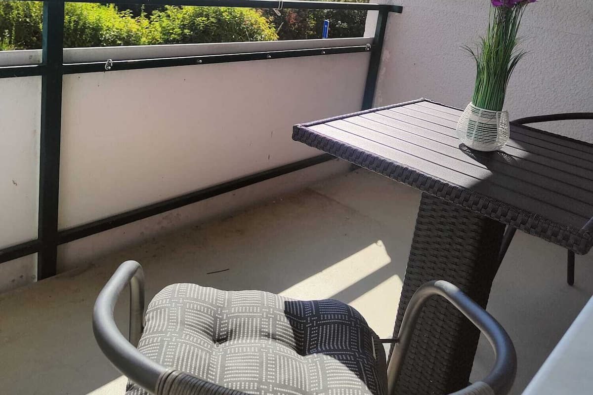 Uma varanda com mesa e cadeiras, um vaso com flores e vista para vegetação e colinas.