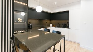 Cozinha moderna com ilha central, armários pretos e bancada de aço inoxidável.